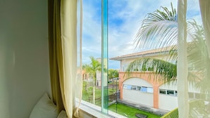 Quarto com uma grande janela que dá para um pátio com palmeiras e um edifício de tijolos.