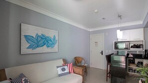 Uma sala de estar com sofá, poltrona, quadro e uma pequena cozinha equipada com micro-ondas.