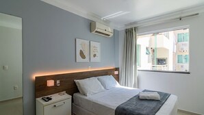 Quarto de hotel com cama, mesa de cabeceira, ar condicionado na parede e janela com vista para edifícios.