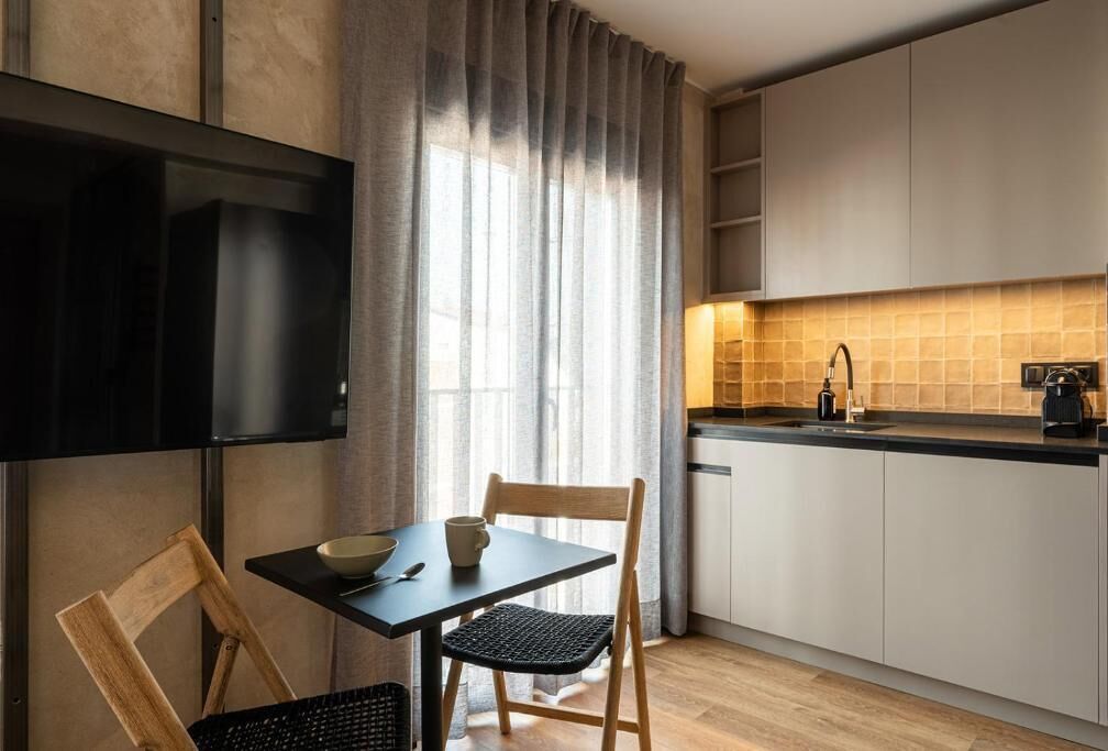 Cozinha compacta com área de refeições, incluindo mesa, cadeiras e uma TV fixada na parede.