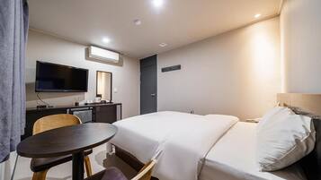Quarto de hotel com uma cama, uma escrivaninha com computador, uma televisão e uma cadeira.