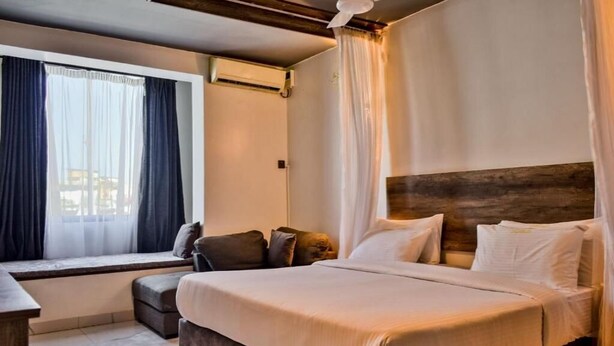 Um quarto com uma cama grande, um assento junto à janela e um ventilador de teto.