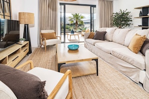 Uma sala de estar moderna com sofá, poltronas, mesa de centro, televisão e varanda com plantas.
