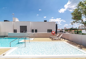 Piscina no terraço com céu claro, espreguiçadeiras e um flutuador.