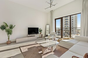 Uma sala de estar moderna com televisão de tela plana, um sofá, uma mesa de centro e uma janela ampla com vista para um edifício.