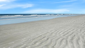Uma praia arenosa com ondas suaves e céu claro.