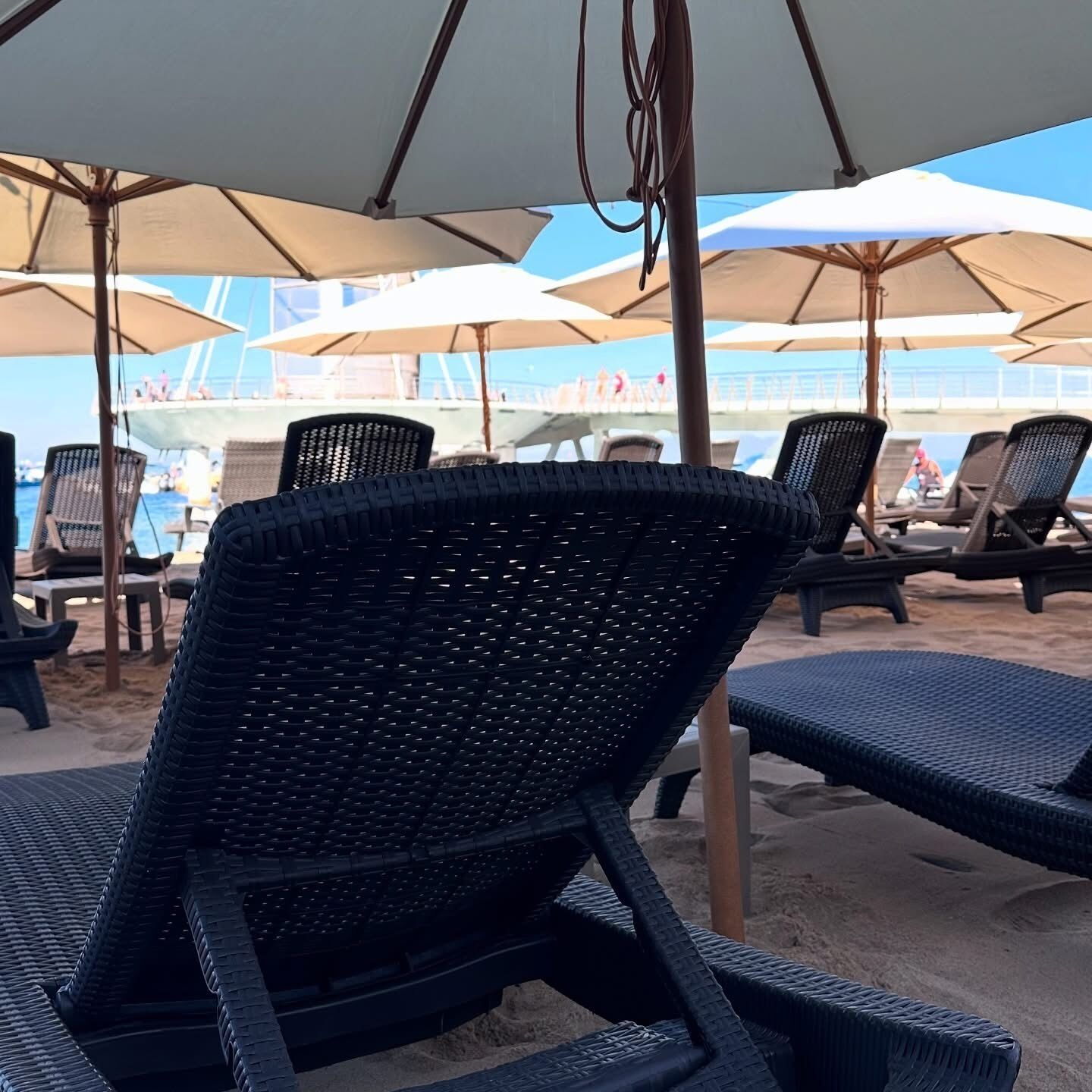 Uma área de descanso à beira-mar, com espreguiçadeiras de vime e guarda-sóis.