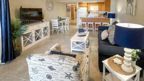 Uma sala de estar com sofá, mesa de centro, televisão e área de jantar com cadeiras e mesa.