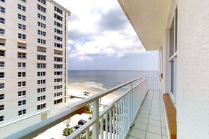 Uma varanda com vista para uma praia e um edifício alto.