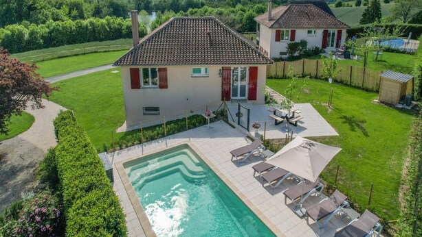 Uma casa com piscina, um alpendre com cadeiras de descanso e um quintal cercado.