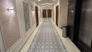 Um corredor com carpete estampado, várias portas e uma lixeira.