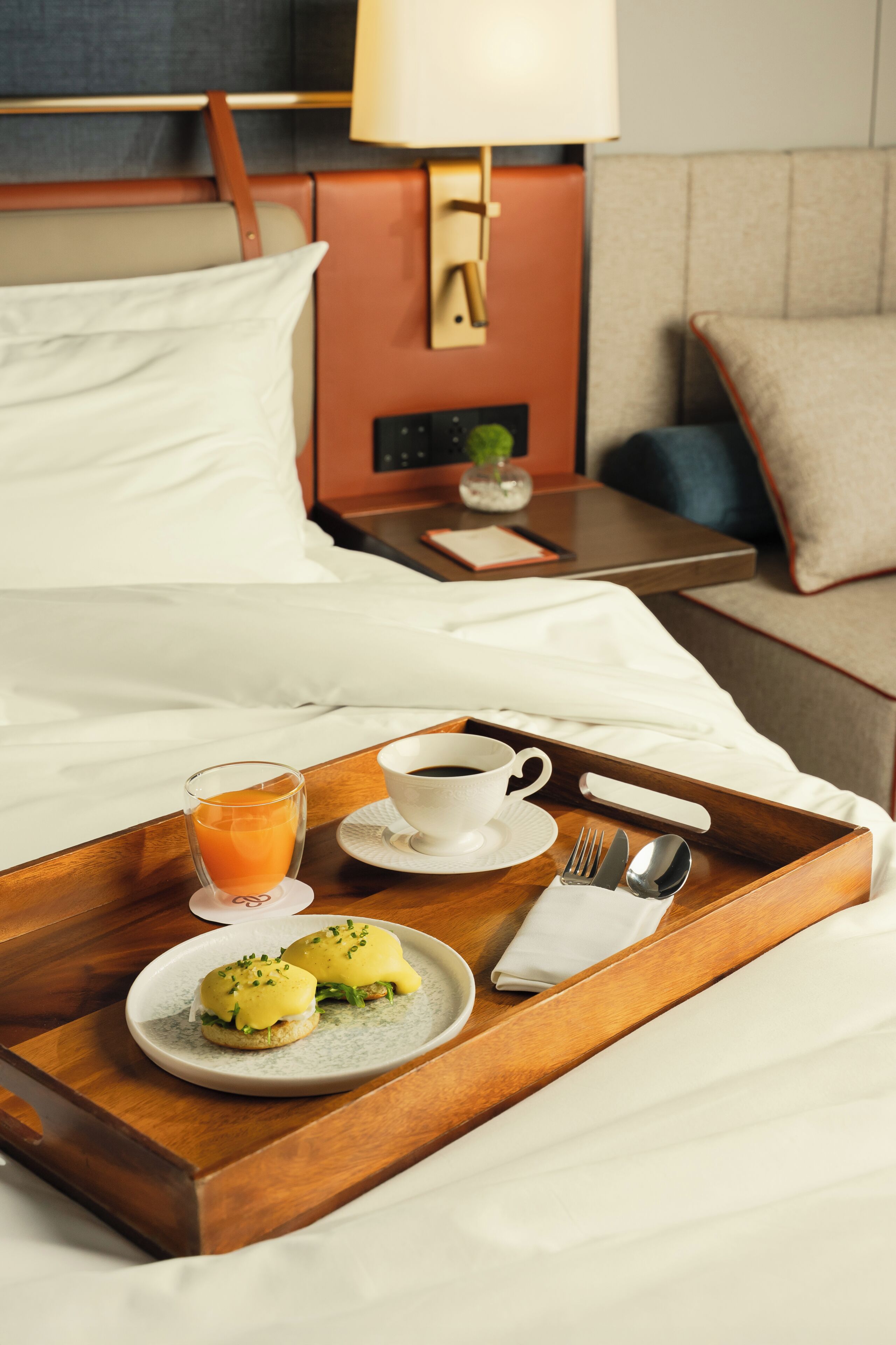Cama bem arrumada com uma bandeja de café da manhã, incluindo ovos Benedict, um copo de suco de laranja e uma xícara de café.