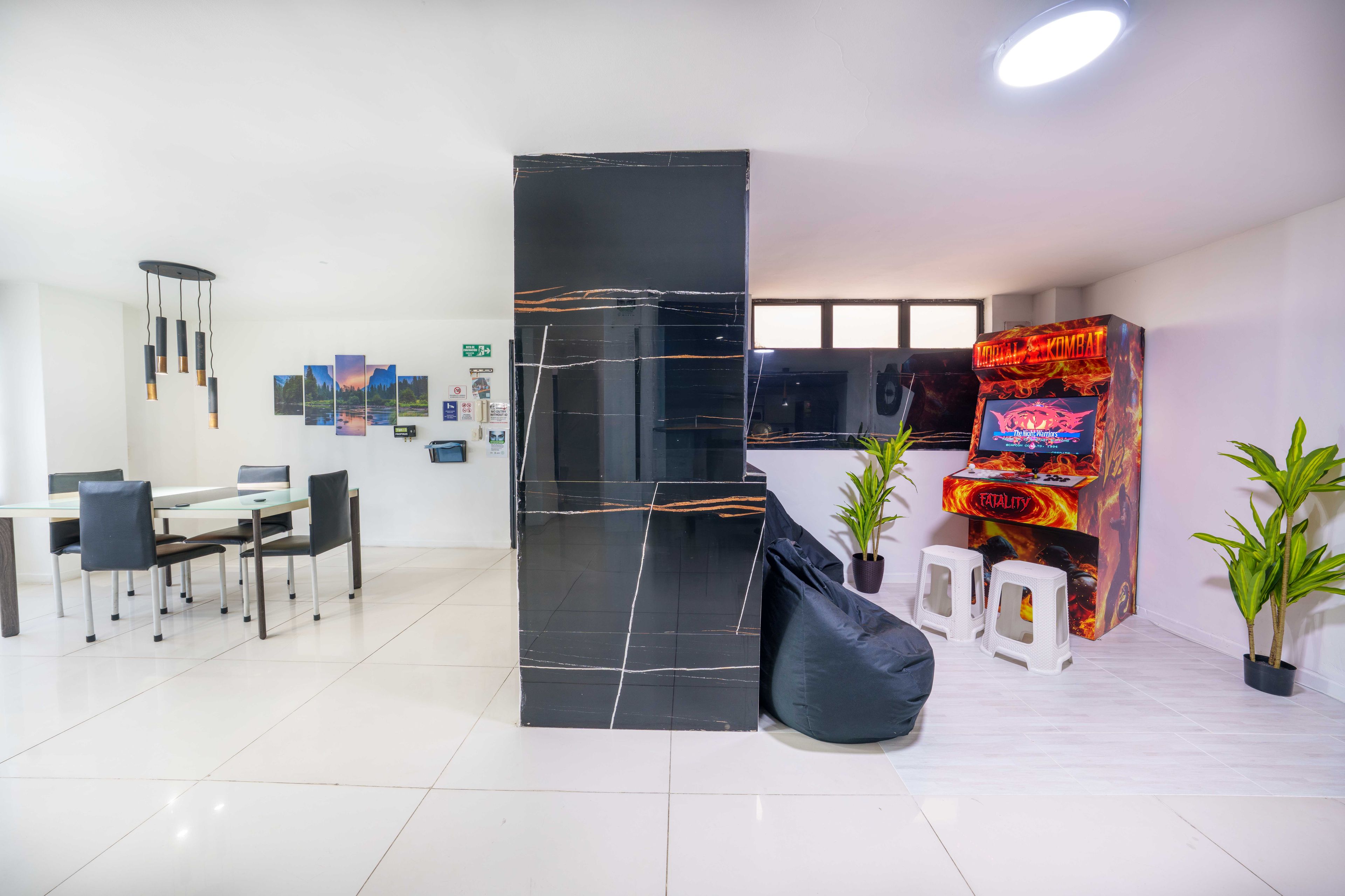 Interior moderno com coluna de mármore preto, máquina de jogos e área de jantar com cadeiras e mesa.