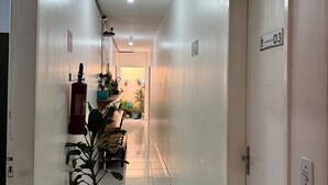 Um corredor com piso de azulejos, plantas em vasos, um extintor de incêndio e uma porta com a inscrição "03".