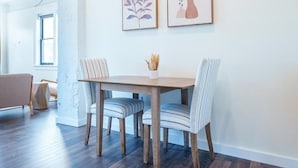 Uma área de refeições com mesa de madeira e cadeiras listradas, duas obras de arte emolduradas na parede e uma janela que oferece iluminação natural.