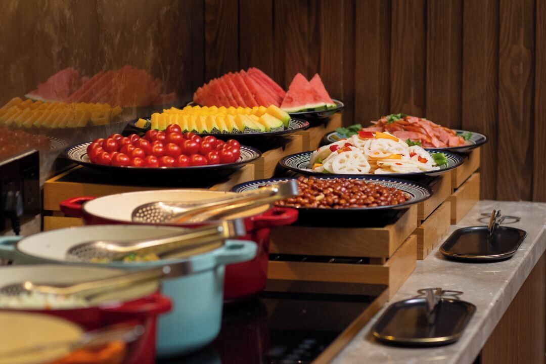 Buffet com diversos pratos, incluindo frutas fatiadas, legumes e carnes.