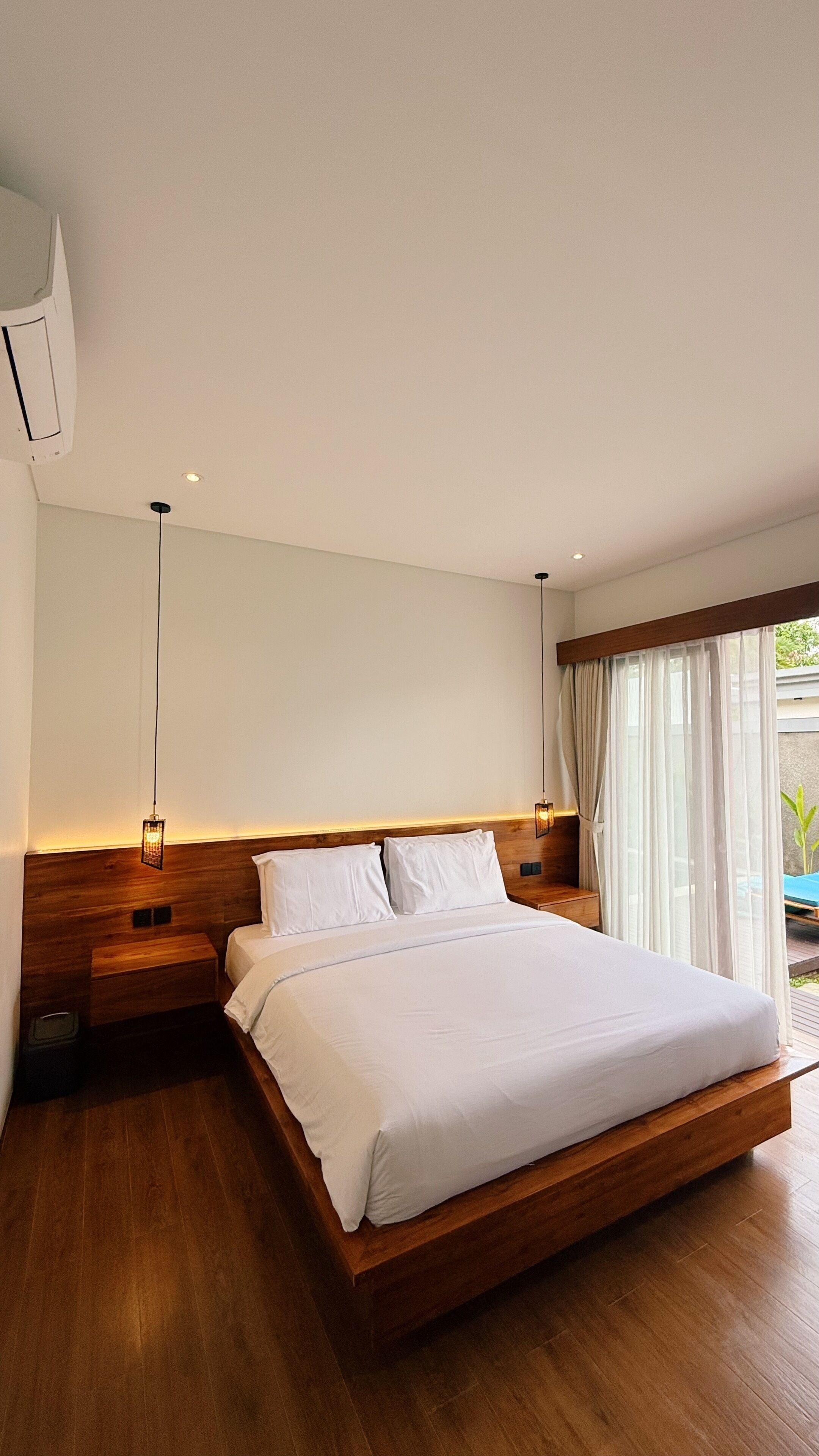 Um quarto moderno com estrutura de cama de madeira, roupa de cama branca e uma mesa de cabeceira com abajur.