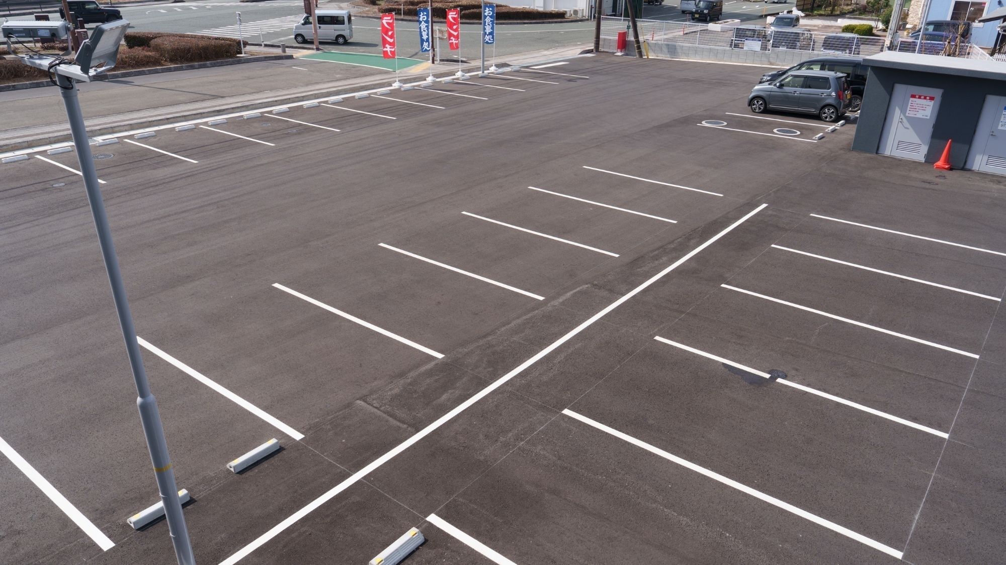 Um parque de estacionamento com vagas demarcadas, uma passadeira e um edifício com sinalética.