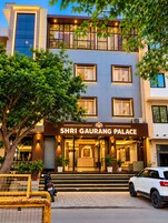 Um hotel de vários andares com uma entrada imponente, uma escadaria que leva à entrada principal e um veículo estacionado na frente.