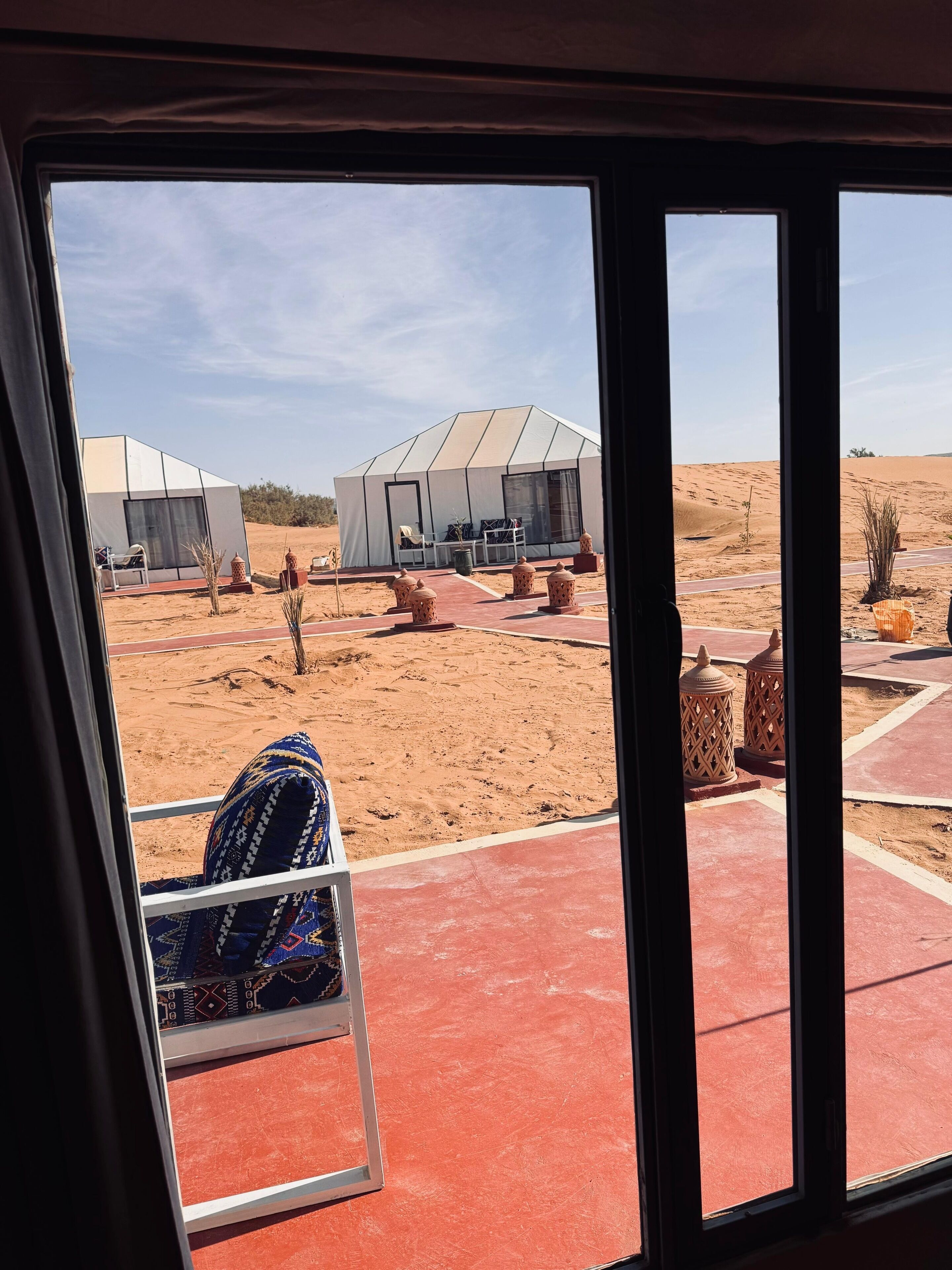 Vista do deserto com uma grande estrutura em forma de tenda, um caminho vermelho e uma cadeira com capa estampada.