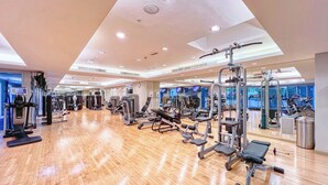 Uma academia ampla com diversos equipamentos de ginástica, piso de madeira e grandes janelas.