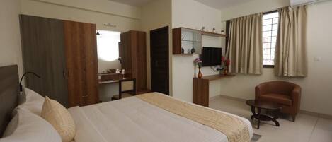 Quarto com cama, escrivaninha, cadeira e televisão.