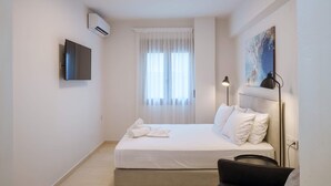 Quarto de hotel com cama, televisão de tela plana, ar condicionado, janela com cortinas leves e um quadro na parede.