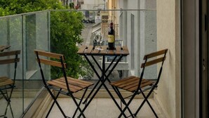 Uma varanda com mesa e cadeiras, dando para uma rua estreita com edifícios.