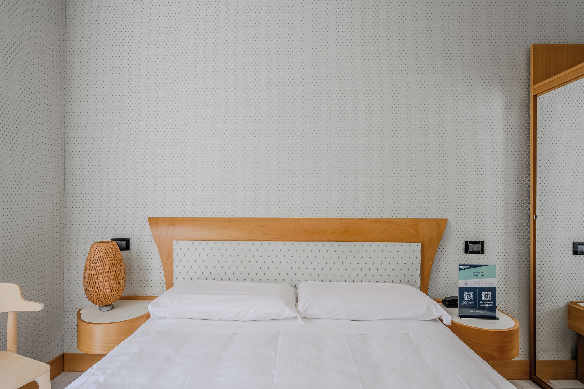 Quarto de hotel com cama, mesa de cabeceira, abajur e placa indicando quarto de temporada.