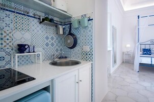 Uma cozinha com pia, fogão e panelas penduradas. Apresenta um balcão branco e um revestimento de parede estampado.