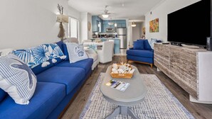 Uma sala de estar moderna com um sofá azul, uma mesa de centro e uma TV sobre um móvel de madeira.