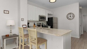 Uma cozinha moderna com armários brancos, uma ilha central com banquetas, eletrodomésticos de aço inoxidável e um relógio de parede.