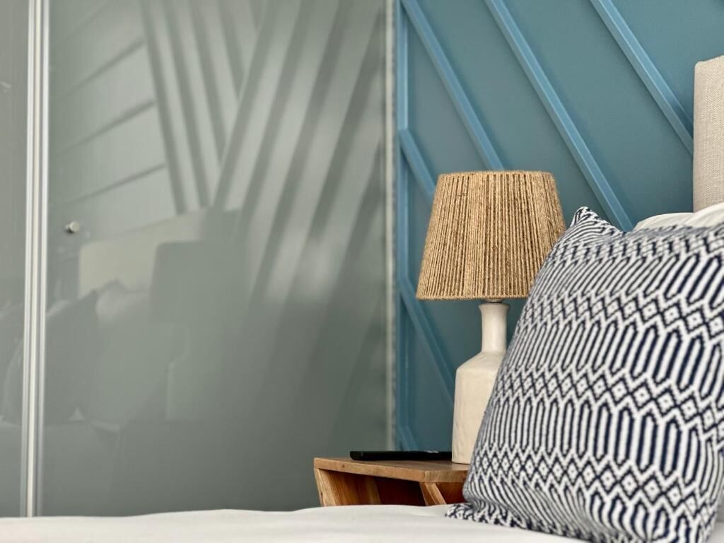 Quarto com cama, mesa de cabeceira e abajur, além de um travesseiro estampado.
