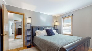 Quarto com cama grande, mesa de cabeceira, abajur e vista para um corredor.