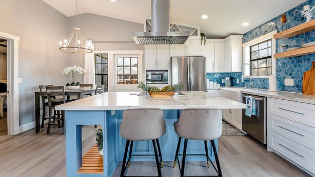 Cozinha moderna com uma ilha grande, eletrodomésticos de aço inoxidável e uma parede azul de destaque.