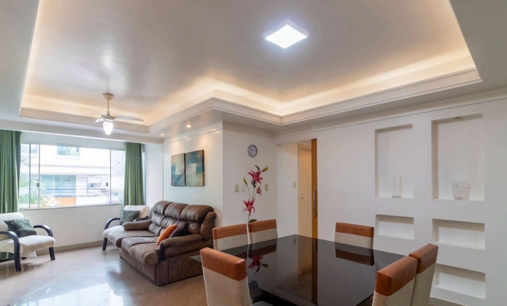 Uma sala de estar moderna com um sofá, uma mesa de jantar com cadeiras, uma luminária no teto e uma janela com cortinas.