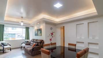 Uma sala de estar moderna com um sofá, uma mesa de jantar com cadeiras, uma luminária no teto e uma janela com cortinas.