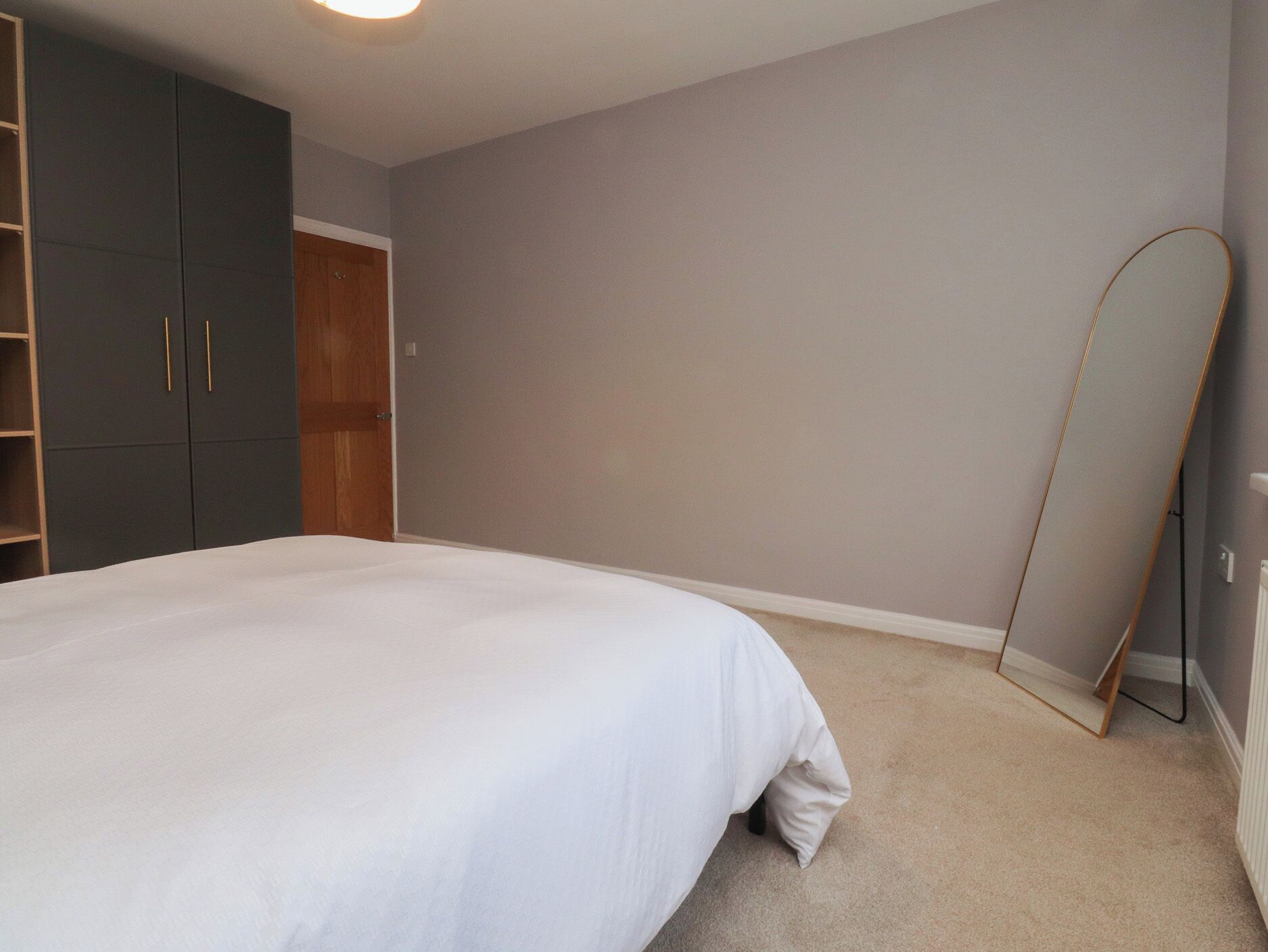 Quarto com cama, guarda-roupa e espelho de corpo inteiro.