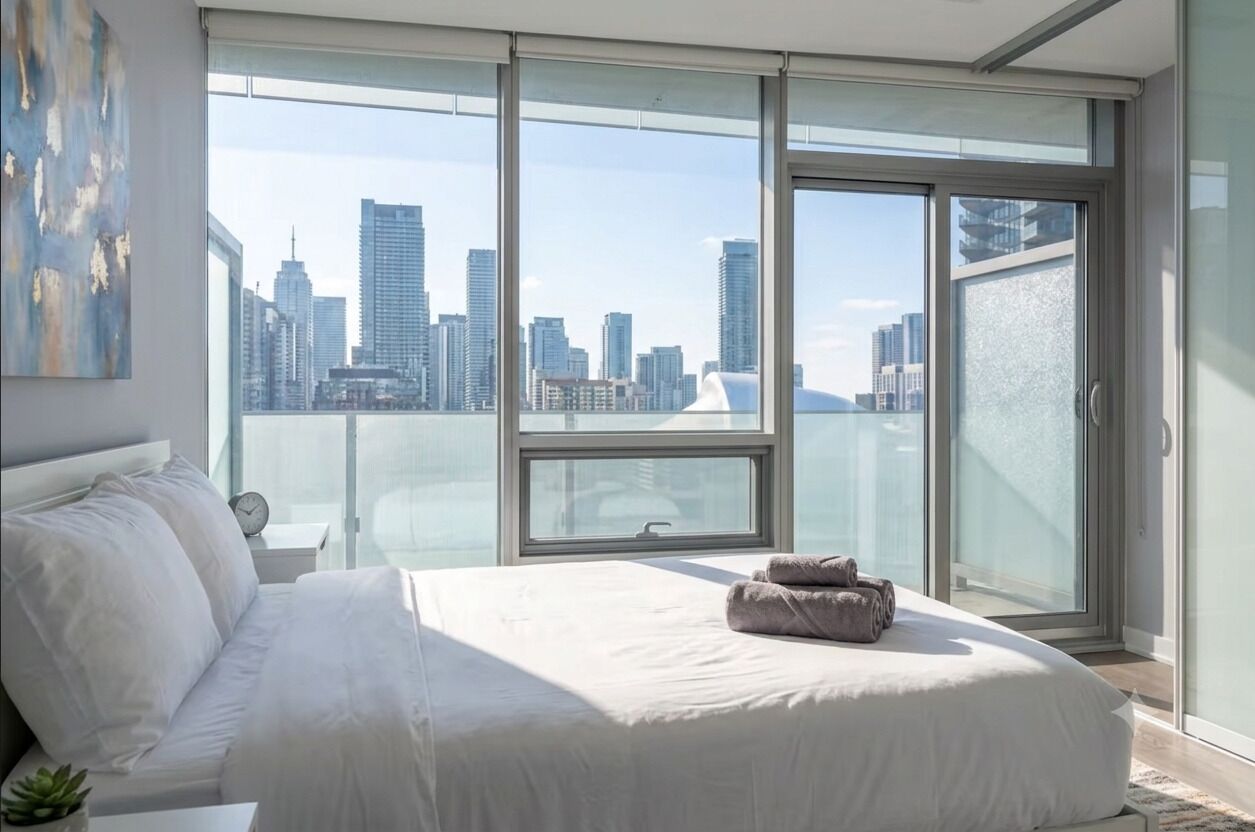Quarto com cama grande, vista da cidade através de janelas do chão ao teto e design moderno.