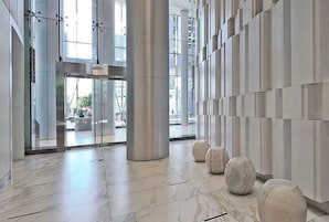 Um lobby moderno com piso de mármore, colunas imponentes e entrada de vidro.