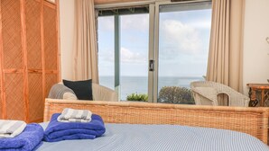 Quarto com cama grande, uma cadeira de vime e vista para o mar.
