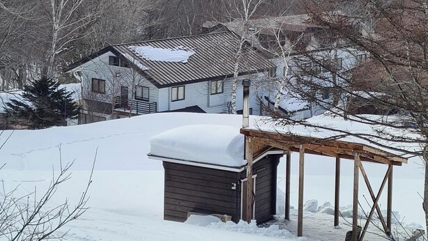 Paisagem coberta de neve com uma cabana e montanhas ao fundo.
