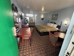 Quarto de hotel com cama, escrivaninha, cadeira, mesinha, espelho, abajur e um quadro na parede.