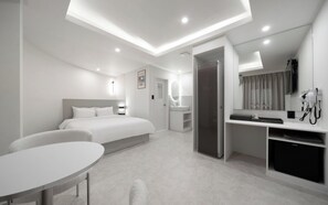 Quarto de hotel moderno com cama, mesa de cabeceira e área de trabalho com espelho.