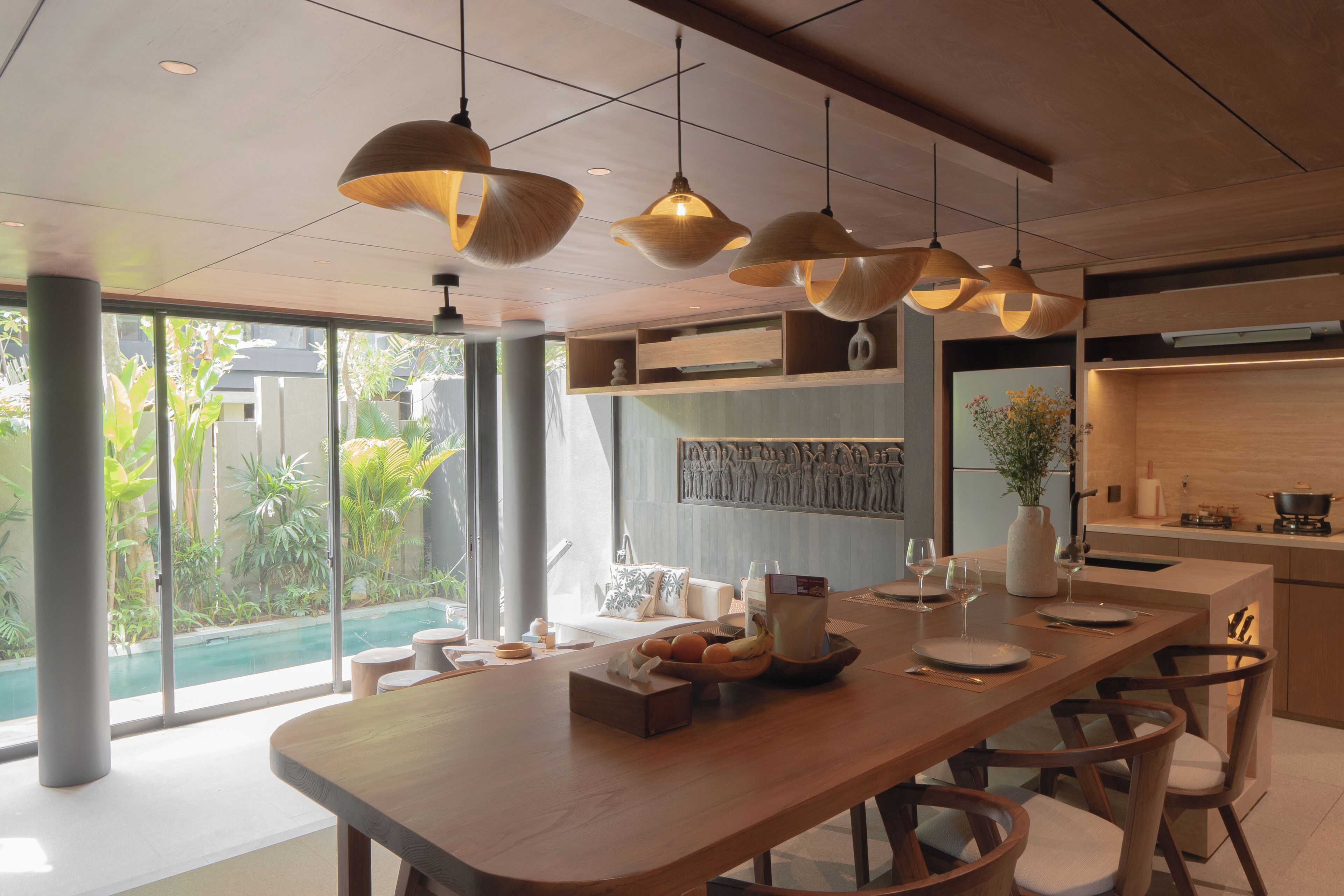 Cozinha moderna com ilha de madeira, iluminação pendente e vista para uma piscina.