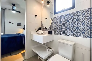 Casa de banho moderna com lavatório branco, um porta-toalhas, sanita e painel de azulejos estampado.