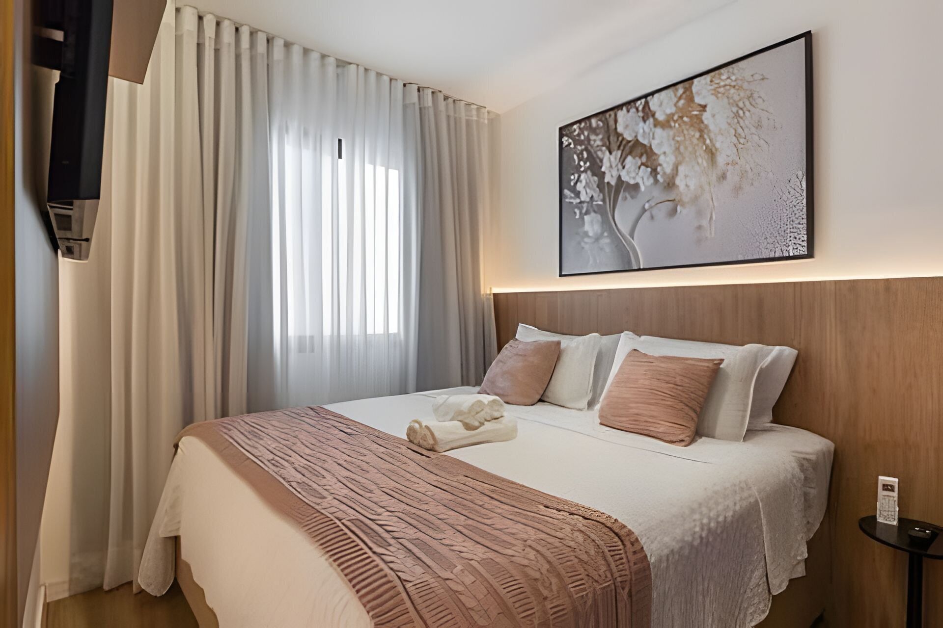 Quarto de hotel com cama, cortinas, um quadro e uma mesa de cabeceira.