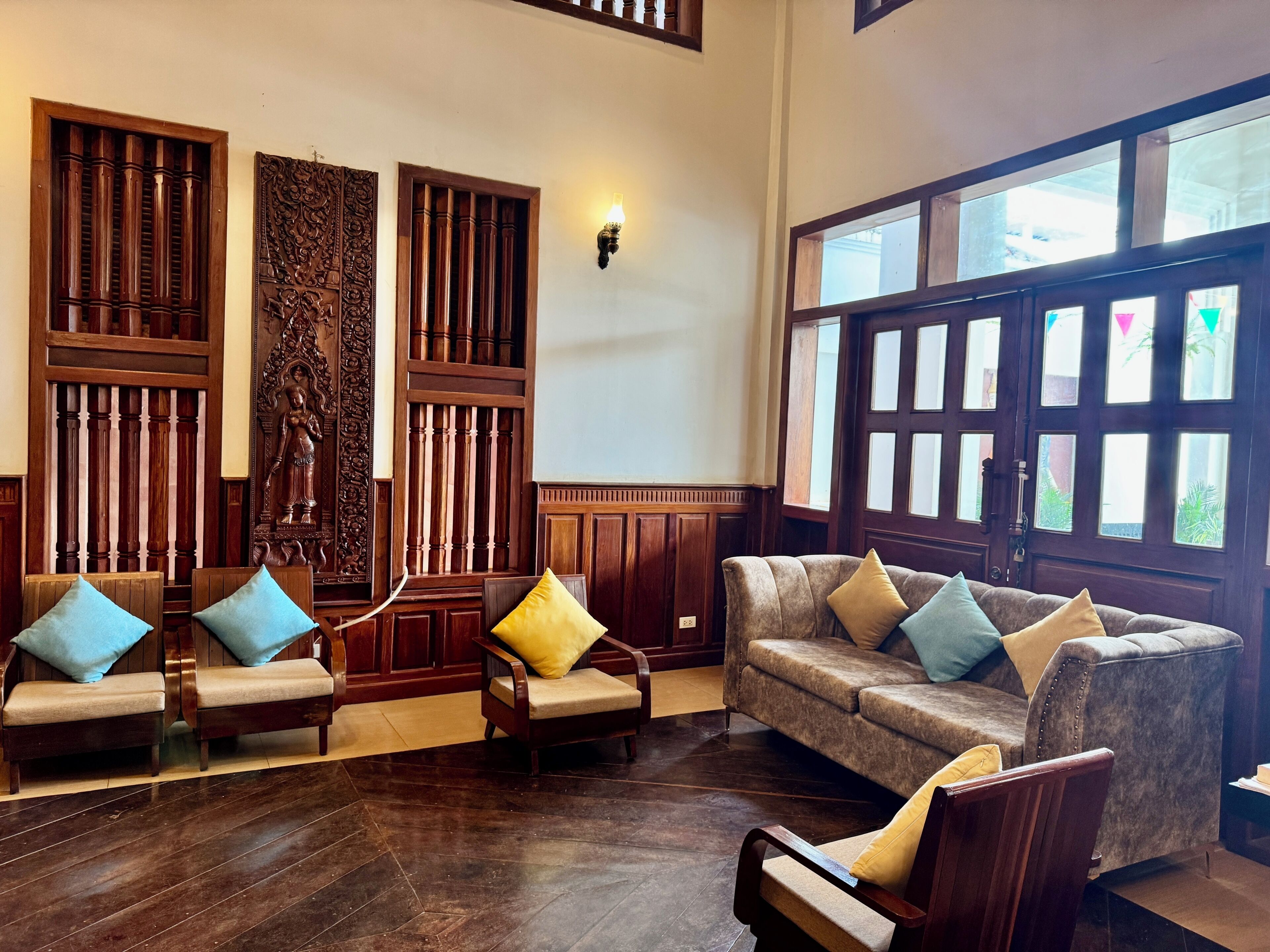 Quarto com piso de madeira, um sofá, um painel decorativo na parede e uma grande janela com vários painéis.