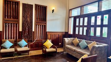 Quarto com piso de madeira, um sofá, um painel decorativo na parede e uma grande janela com vários painéis.