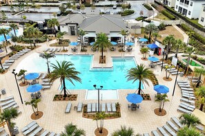 Uma área de piscina no terraço com espreguiçadeiras, guarda-sóis e palmeiras.